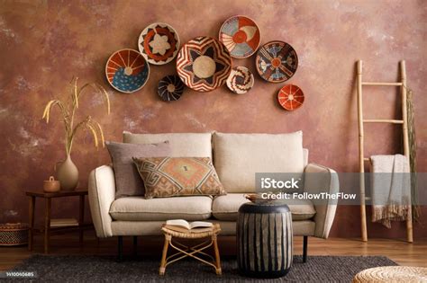 디자인 베이지 색 소파 커피 테이블 의자 고리 버들 바구니 및 개인 액세서리가있는 거실 인테리어의 세련된 보호 퇴비 갈색과 흰색 베개와 격자무늬 아늑한 아파트 가정 장식