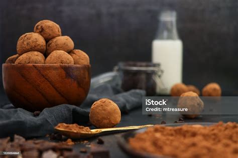 가나슈 센터가 있는 수제 개별 초콜릿 트러플 과자 회색 티타월 금속 숟가락 우유 병 짙은 회색 배경 전경에 초점을 맞춘 나무 그릇에 코코아 파우더를 더럽힌 고급 초콜릿 볼