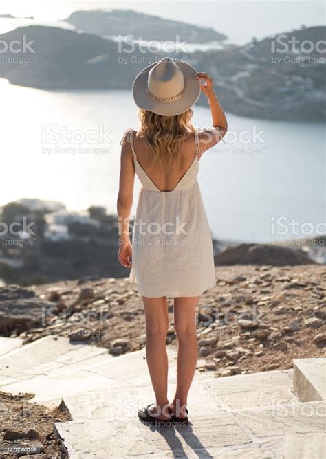 하얀 드레스와 모자를 쓴 젊은 여성이 계단에 서서 경치를 즐기고 있다 이오스 그리스 계단 및 층계에 대한 스톡 사진 및 기타 이미지 계단 및 층계 관광 리조트 뒤