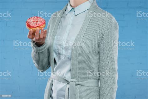 자른 스웨터와 셔츠 블루 벽돌 벽 앞 맛 있는 유약된 도넛을 들고 있는 여자의 샷 건강에 좋지 않은 음식에 대한 스톡 사진 및