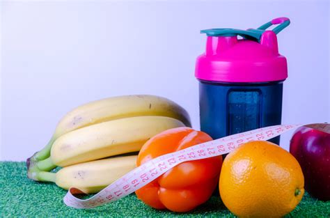 분홍색 모자가있는 파란색 병 녹색 잔디에 스포츠 영양을 위한 셰이커 바나나 빨간 사과 오렌지 피망 흰색 배경의 오렌지 다이어트가있는 테이프를 측정했습니다 0명에 대한 스톡