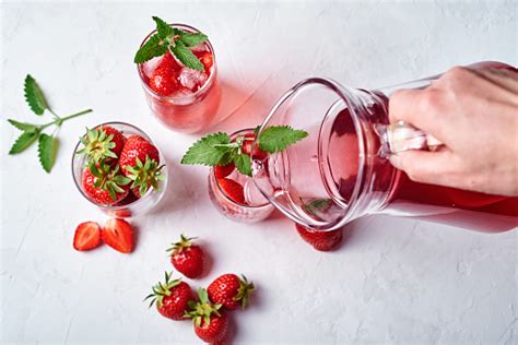 흰 배경에 유리로 용기에서 레모네이드를 붓는 여자 테이블에 딸기 얼음과 민트와 칵테일 공간을 복사합니다 추운 여름 베리 음료