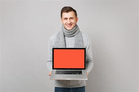회색 스웨터 스카프 빈 빈 화면 회색 배경에 고립 된 노트북 Pc 컴퓨터를 들고 웃는 젊은 남자가 있다 건강 온라인 치료 컨설팅 추운 계절 개념 복사 공간을 비웃는 다