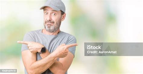 잘생긴 중 년 노인의 수석 남자 이상 스포츠 모자를 쓰고 절연 배경 손가락으로 양쪽 모두를 가리키는 다른 방향 반대 가리키기에 대한 스톡 사진 및 기타 이미지 Istock