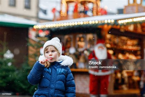 크리스마스 시장에 과자 가판대에서 사탕 지팡이를 가진 귀여운 미취학 소녀 독일의 전통적인 가족 시장에서 행복한 아이 눈이 내리는 동안 화려한 겨울 옷을 입은 미취학 아동