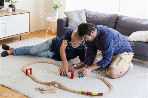 선배 아버지와 성인 아들은 행복하고 미소로 집에서 함께 장난감 나무로 놀고 있습니다 거실에서 바닥에 장난감 자동차와 함께 노는 두 남자 2명에 대한 스톡 사진 및 기타