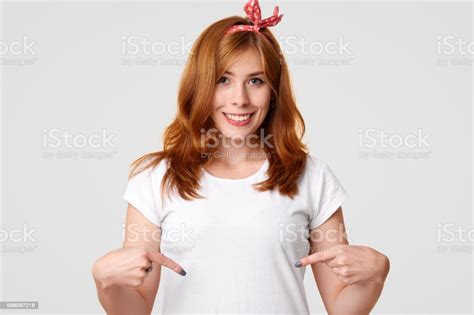 캐주얼 화이트 티셔츠와 머리 띠 기쁘게 사랑 스러운 젊은 여자의 수평 총 만족도 다운 포인트 미소 긍정적으로 보여줍니다 뭔가 바닥에 사람과 광고 개념 T 셔츠에 대한 스톡