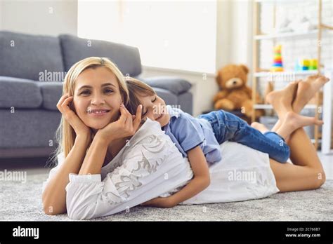 Schöne junge Mutter und ihr Sohn liegen auf weichem Teppich zu Hause Niedlich junge umarmt