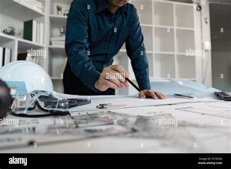 Engineer Analyzing Architectural Blueprints In Modern Office Setting With Tools And Safety Gear