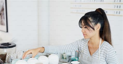 작업복을 입은 젊은 아시아 여성이 커피 머신 옆에 서 있는 동안 쟁반에 깨끗한 컵을 올려놓는다 사진 Unsplash의 러시아 이미지