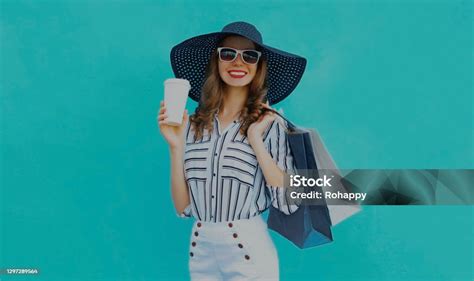 파란색 배경에 검은 둥근 여름 모자를 쓰고 쇼핑 백과 커피 컵을 가진 아름다운 행복한 미소 여자의 초상화 생활 방식에 대한 스톡 사진 및 기타 이미지 Istock