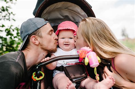 행복 한 가족 엄마 아빠 외부 딸 키스 어머니 아기 캐리지에 아버지 키스 소녀 행복 한 남성과 여성은 배경 자연에 유모차에 아이 들과 함께 연주 가족에 대한 스톡 사진 및