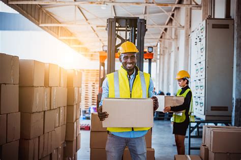 민속 트럭이 공장 창고를 계속 보관할 수 있도록 농산물 상자를 옮기는 데 도움을 주는 업계 종사자들은 안전 복을 입고 일합니다 2명에 대한 스톡 사진 및 기타 이미지