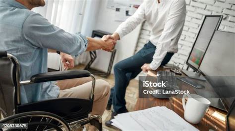 좋은 거래 창의적인 사무실에서 함께 일하는 동안 휠체어를 타고 동료에게 악수를 하는 남성 사무직 근로자의 시야를 잘라냈습니다 건강관리와 의술에 대한 스톡 사진 및 기타