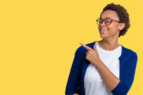 손과 얼굴에 행복 하 고 자연 식 가진 측까지 손가락으로 가리키는 얼굴의 미소와 쾌활 한 고립 된 배경 위에 안경을 쓰고 젊은 아름 다운 아프리카계 미국인 여자 가리키기에