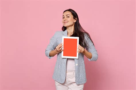 분홍색 파스텔 배경에 고립 된 빈 빈 화면으로 태블릿 Pc 컴퓨터를 들고 줄무늬 재킷에 예쁜 젊은 여자의 초상화 사람들은 진심으로 감정 라이프 스타일 개념입니다 복사 공간을