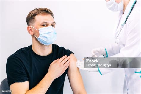 안전 마스크와 보호 장갑을 착용한 여성 간호사가 코로나19 팬데믹 기간 동안 의료 센터에서 남성 환자에게 백신 주사를 맞고 있다