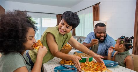 행복한 아프리카 가족 부모와 두 어린 딸이 함께 프라이드 치킨과 피자를 먹고 있습니다 아버지와 어머니와 귀여운 아이 소녀 아이는 집에서 함께 먹고 식사를 나누는 것을