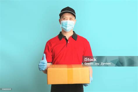 빨간 셔츠 유니폼 얼굴 마스크 장갑배달남자 직원은 파란색 배경에 빈 골판지 상자를 들고 있다 코로나 바이러스 2019 개념