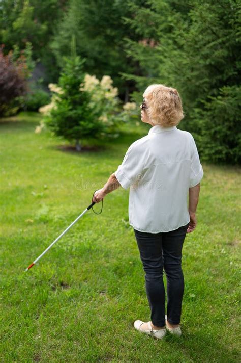 An Elderly Blind Woman Walks With A Cane Along A Tactile Tile Stock