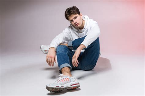 흰색 스웨트 셔츠 청바지와 흰색 운동화를 입고 유행 잘 생긴 젊은 유럽 남성 모델은 상업 사진 촬영을위한 분홍색 배경에 스튜디오에서 포즈를 취하고 카메라를보고 놀이에 대한