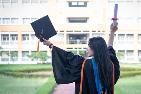 행복하고 흥분한 젊은 아시아 여성 대학 졸업생의 초상화는 졸업 가운을 입고 졸업당일 대학 캠퍼스에서 학위를 받은 모자를 쓰고 있습니다 교육 개념 계획에 대한 스톡 사진 및