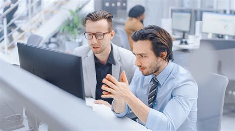 밝은 현대 사무실에서 잘 생긴 사무실 노동자 앉아서 그의 데스크톱 컴퓨터에서 작업 그의 남성 프로젝트 관리자와 문제 해결에 대해