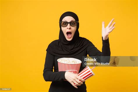아라비아 무슬림 여성 히 잡 블랙 옷 3d 아이맥스 안경 시계 영화 필름 개최 팝콘 소 다 컵 노란 벽 배경 스튜디오 초상화에 고립 사람들 라이프 스타일 개념입니다 복사