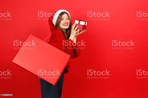 크리스마스와 새해 쇼핑 빨간 배경에 패키지와 선물을 가진 산타의 모자를 쓴 예쁜 젊은 여자 25 29세에 대한 스톡 사진 및