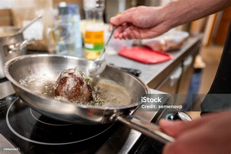 셰프가 반짝이는 팬에 그을린 스테이크를 굽고 버터와 허브로 풍미를 더합니다 이 이미지는 활기찬 주방 환경에서 미식가 요리의 복잡한 과정을 포착합니다 고급 요리에 대한 스톡