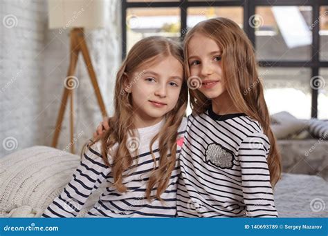 The Image Of Two Little Sisters Sitting On The Bed In The Room Stock
