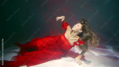 Romantic Blonde Woman Is Stretching Her Body On A Bottom Of Sea Floating Underwater In Red