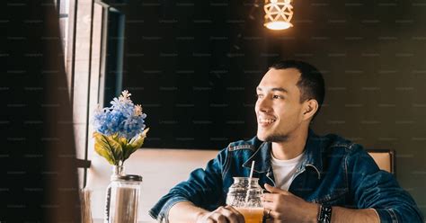 쾌활하고 웃는 젊은 라틴 아메리카 남자가 식당 테이블에서 얼음 음료를 마시고 있다 라이프 스타일 개념 사진 Unsplash