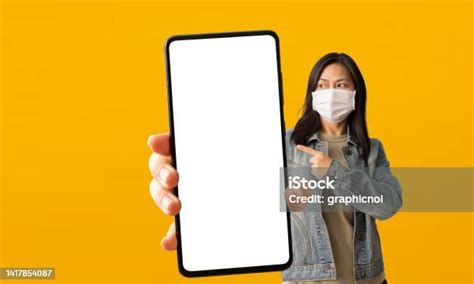 아시아 여성들은 노란색 배경에 큰 스마트 폰을 들고 의료 얼굴 마스크를 착용하고 디자인 작업을위한 격리 된 클리핑 경로 빈 여유 공간 모의 제품 디스플레이 프리젠 테이션을