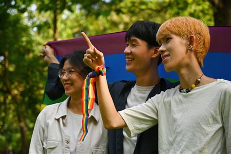 Lgbt 십대 그룹이 자랑스럽게 서서 기대하고 있고 그 중 한 명이 무지개 깃발을 들고 있는 사진 20 24세에 대한 스톡 사진