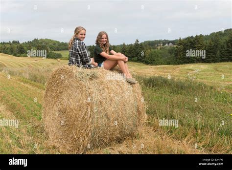 Two Girls Sit On Top Of A Large Hay Bale In A Field Kensington Prince Edward Island Canada