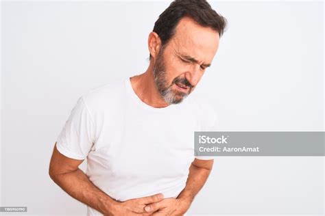 중년 잘생긴 남자는 편안한 흰색 배경 위에 서 있는 캐주얼 한 티셔츠를 입고 위장에 손을 대고 메스꺼움 고통스러운 질병이 좋지 않기 때문에 아쉬 컨셉 남자에 대한 스톡 사진