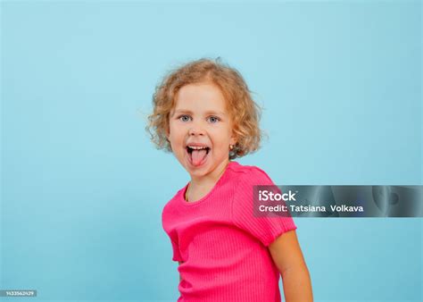 곱슬 머리를보고 혀를 보여주고 푸른 배경에 놀리는 찡그린 파란 눈을 가진 어린 소녀의 초상화 사람 얼굴에 대한 스톡 사진 및 기타 이미지 Istock