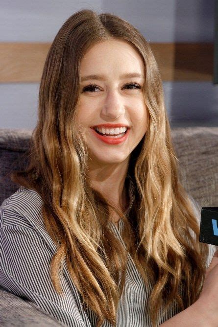 A Woman Sitting On Top Of A Couch Holding A Remote Control In Her Hand And Smiling At The Camera