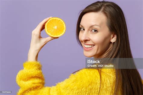 스튜디오에서 보라색 파스텔 배경에 고립 된 신선한 잘 익은 오렌지 과일의 절반 손을 잡고 모피 스웨터에 젊은 여자를 웃는 사람들은 생생한 라이프 스타일 휴식 휴가 개념입니다