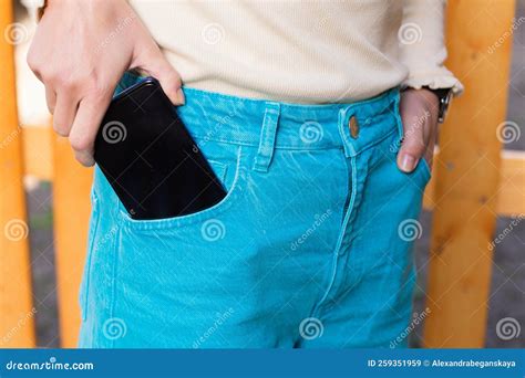 The Girl Puts The Phone In The Front Pocket Of Her Blue Denim Pants
