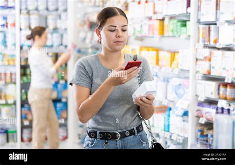 Using Smartphone To Read Information Woman Scans A QR Code On Package Of Cosmetics Stock Photo