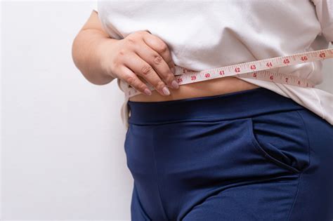 과체중의 징후를 보이는 통통한 여성의 배나 허리 배꼽으로 측정 테이프를 사용하는 동안 여성의 손에 총을 맞춥니다 텍스트에 대한 복사 공간이 있는 흰색 배경에 저울에 대한