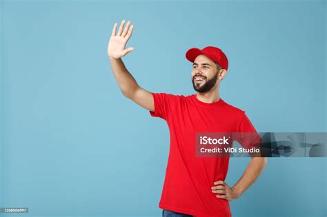 파란색 벽 배경 스튜디오 초상화에 고립 된 빨간색 유니폼 작업복을 입은 배달 남자 택배 딜러로 일하는 캡 티셔츠 프린트의 전문 남성 직원 서비스 개념 복사 공간을 모의합니다