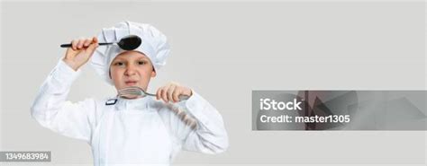 흰색 요리사 유니폼을 입은 작은 행복한 소년의 클로즈업 초상화와 큰 숟가락과 흰색 스튜디오 배경에 고립 된 포크가있는 거대한