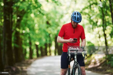 스마트 폰을 들고 화창한 날에는 숲속의 아스팔트 도로에서 자전거를 타는 자전거 빨강에 대한 스톡 사진 및 기타 이미지 빨강