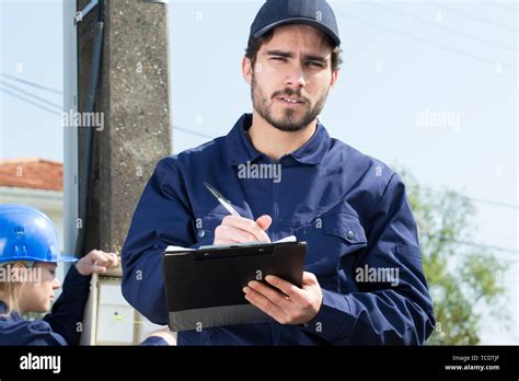 Engineer In Blue Overall Writing On Clipboard By Electric Meter Stock
