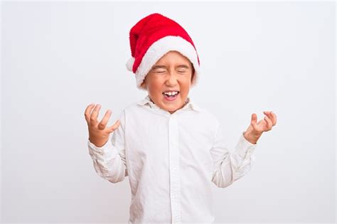 고립 된 흰색 배경 위에 서있는 크리스마스 산타 모자를 쓰고있는 아름다운 아이 소년은 팔을 들고 눈을 감고 흥분을 일으키며 성공을 축하합니다 우승자 컨셉 12월에 대한 스톡
