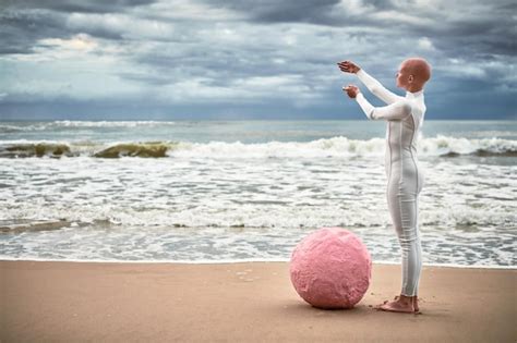 Premium Photo Hairless Girl With Alopecia In White Futuristic Suit Standing On Stone Sea Beach