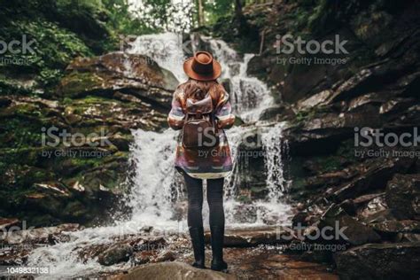 여행과 방 랑 벽 개념입니다 산에 숲에 폭포 보고 배낭 모자에 세련 된 Hipster 소녀 여행자 여자 숲 탐험입니다 여름 휴가 텍스트를 위한 공간 강에 대한 스톡 사진 및
